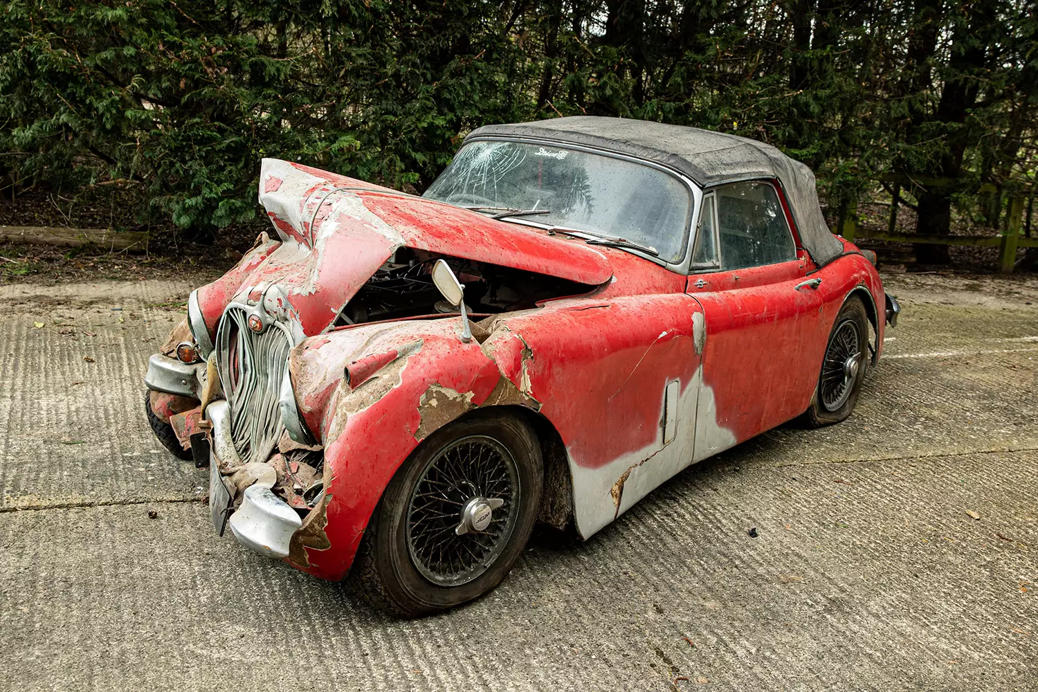 Ein roter Jaguar XK150 von 1960, der gegen einen Baum gefahren ist