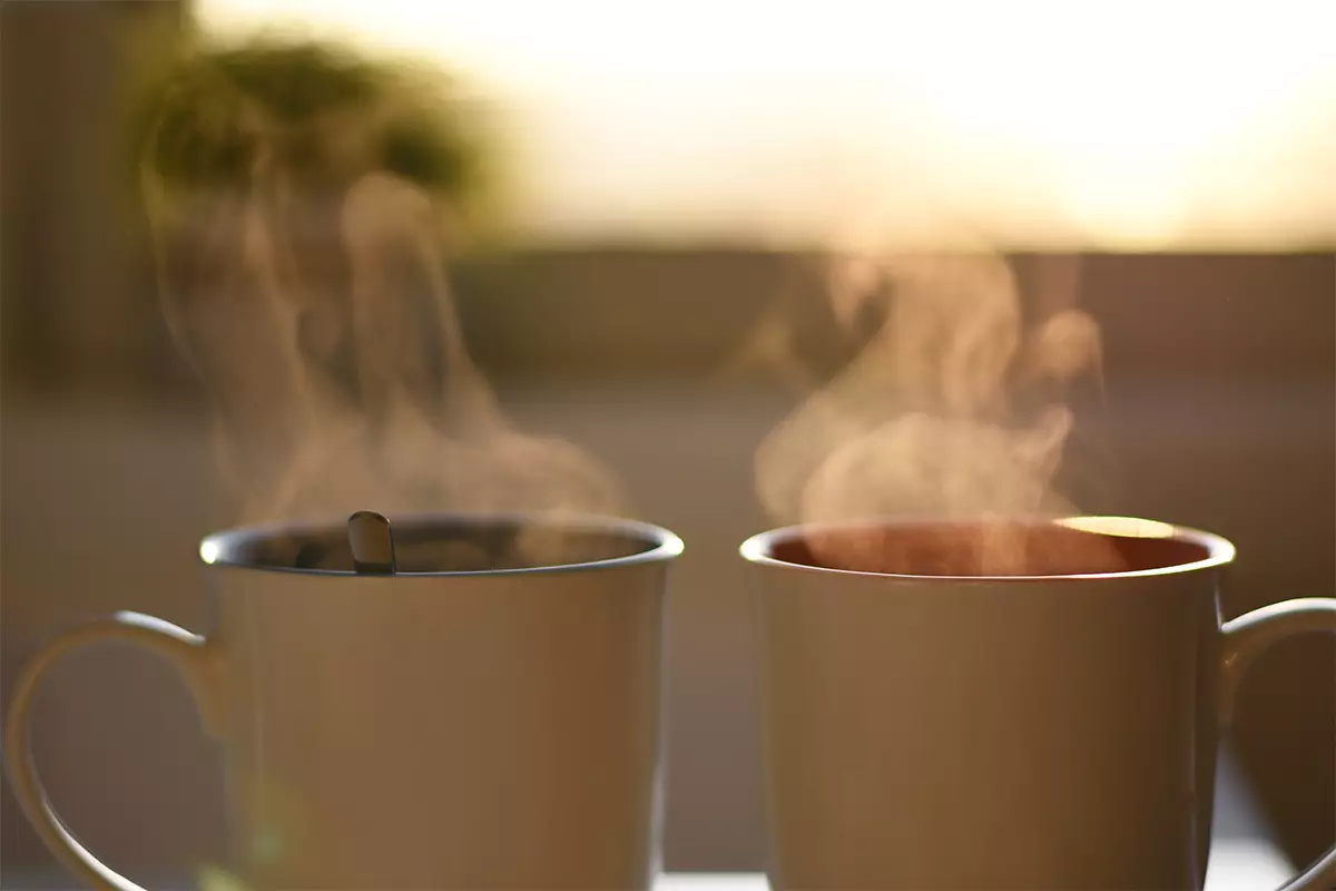 Vapor que surt de dues tasses de cafè amb la sortida del sol al fons