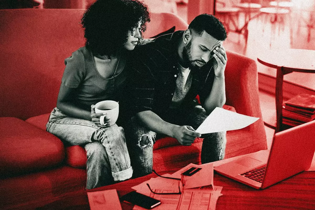 Niewierność finansowa ma miejsce, gdy partner w związku kłamie lub ukrywa swoją sytuację finansową przed partnerem. To zdjęcie pokazuje parę siedzącą razem na kanapie, wyglądającą na zmartwioną, podczas gdy mężczyzna przegląda dokumenty finansowe.