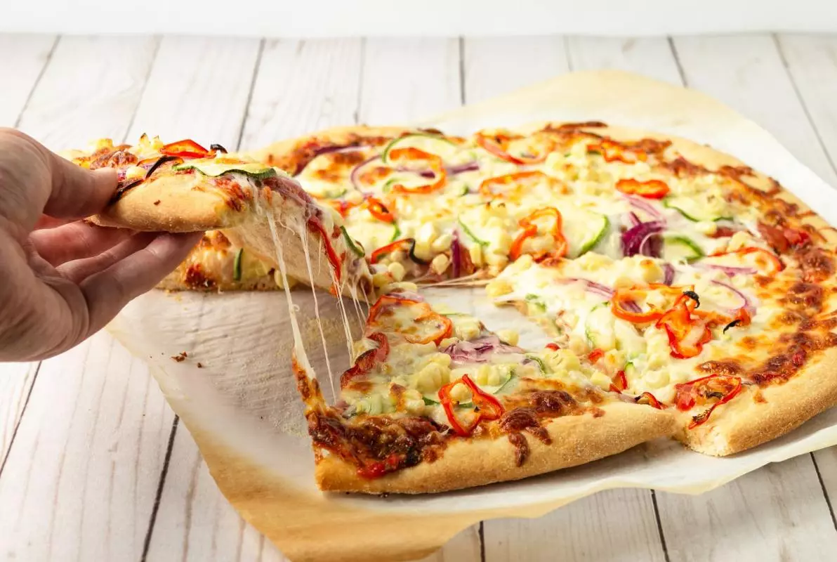 Pizza fuq platt tas-servizz fuq mejda b'id tintlaħaq 'l isfel u tiġbed biċċa 'l bogħod