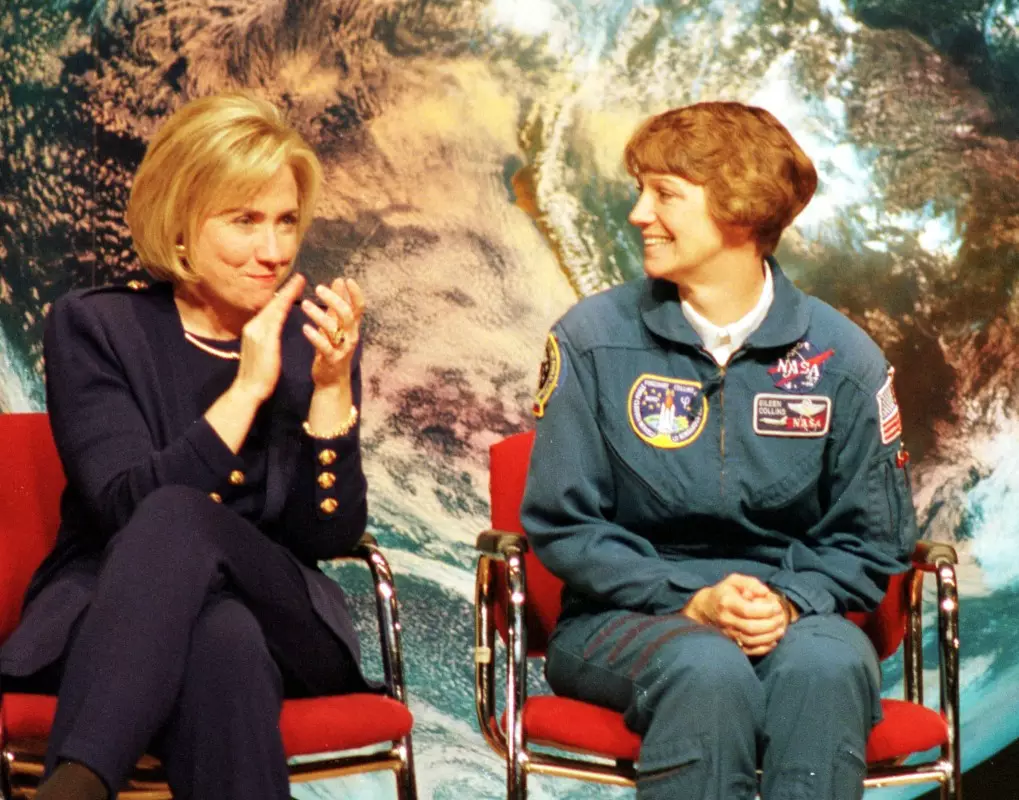 Premye dam Hillary Rodham Clinton (L) bat bravo pou astronot Eileen Collins pandan yon vizit ak etidyan syans nan Dunbar High School 5 mas 1998 nan Washington, DC. Collins te nonmen premye fanm kòmandan yon misyon NASA ki pral lanse an avril 1999. (Foto Karin Cooper)