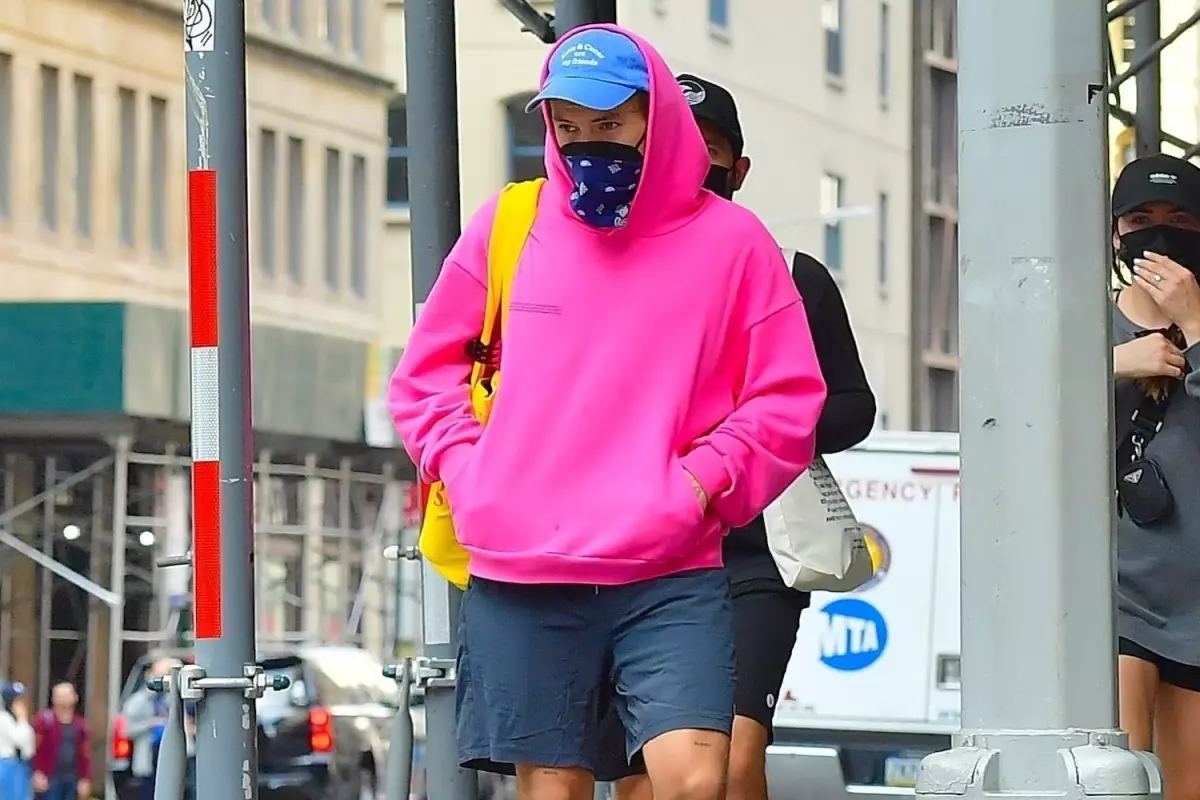 Harry Styles nganggo hoodie pink lan kathok cendhak navy