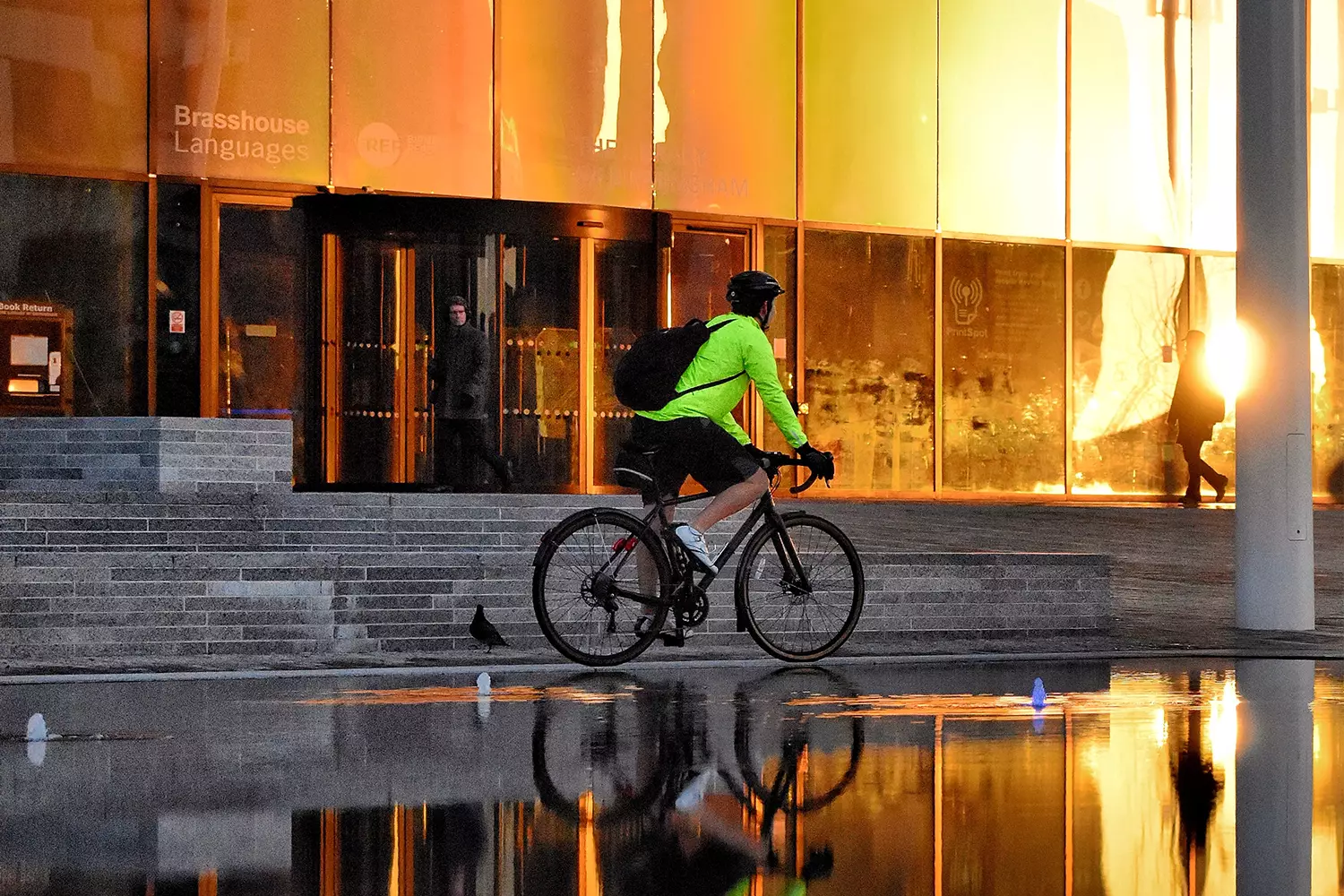 Dojíždějící na kole ve fluorescenční zelené bundě na kole při východu slunce