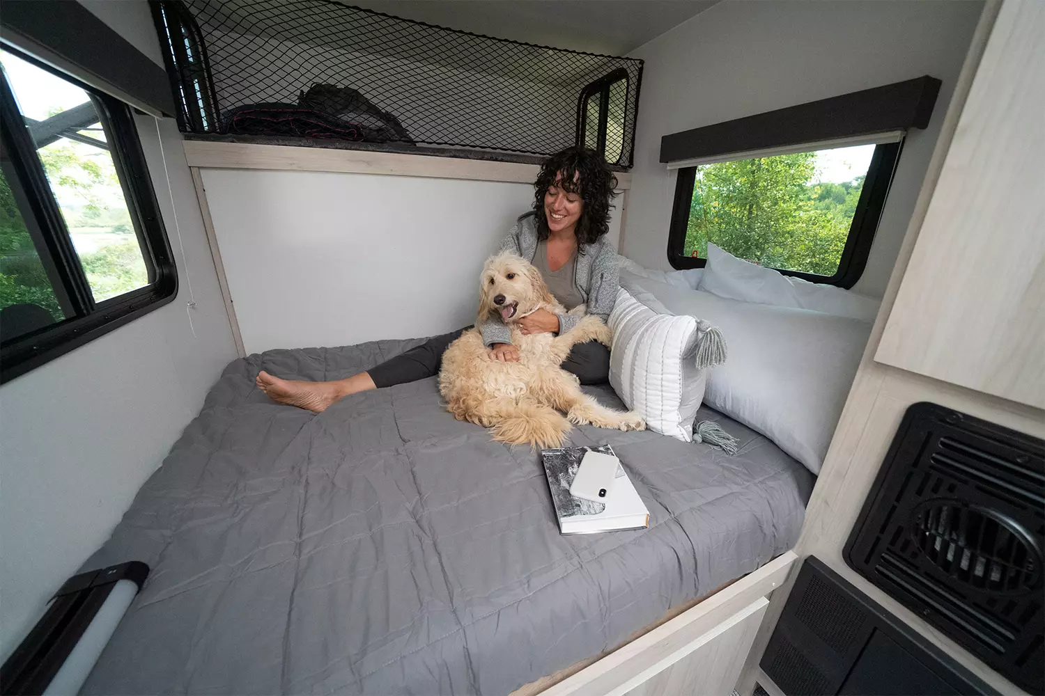 Une femme et son chien assis sur le lit à l'intérieur d'une roulotte Hike 100 de Winnebago