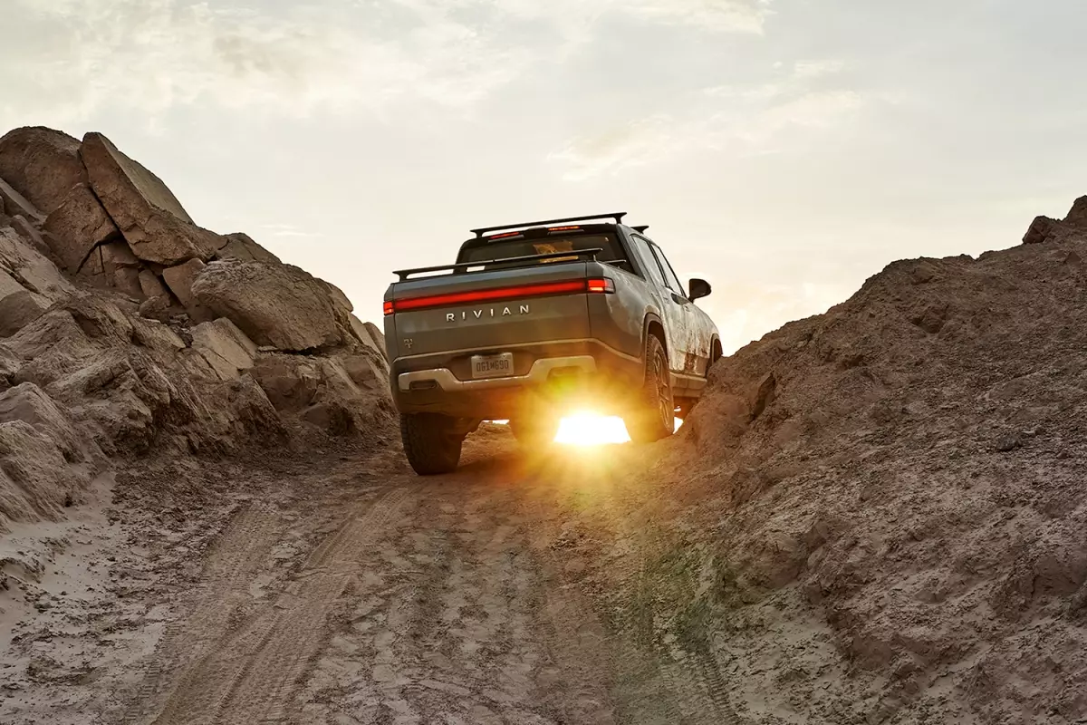 The Rivian R1T treuk pickup listrik ditémbongkeun ti pungkur nyetir ngaliwatan pasir kokotor taringgul nalika Panonpoé Tilelep