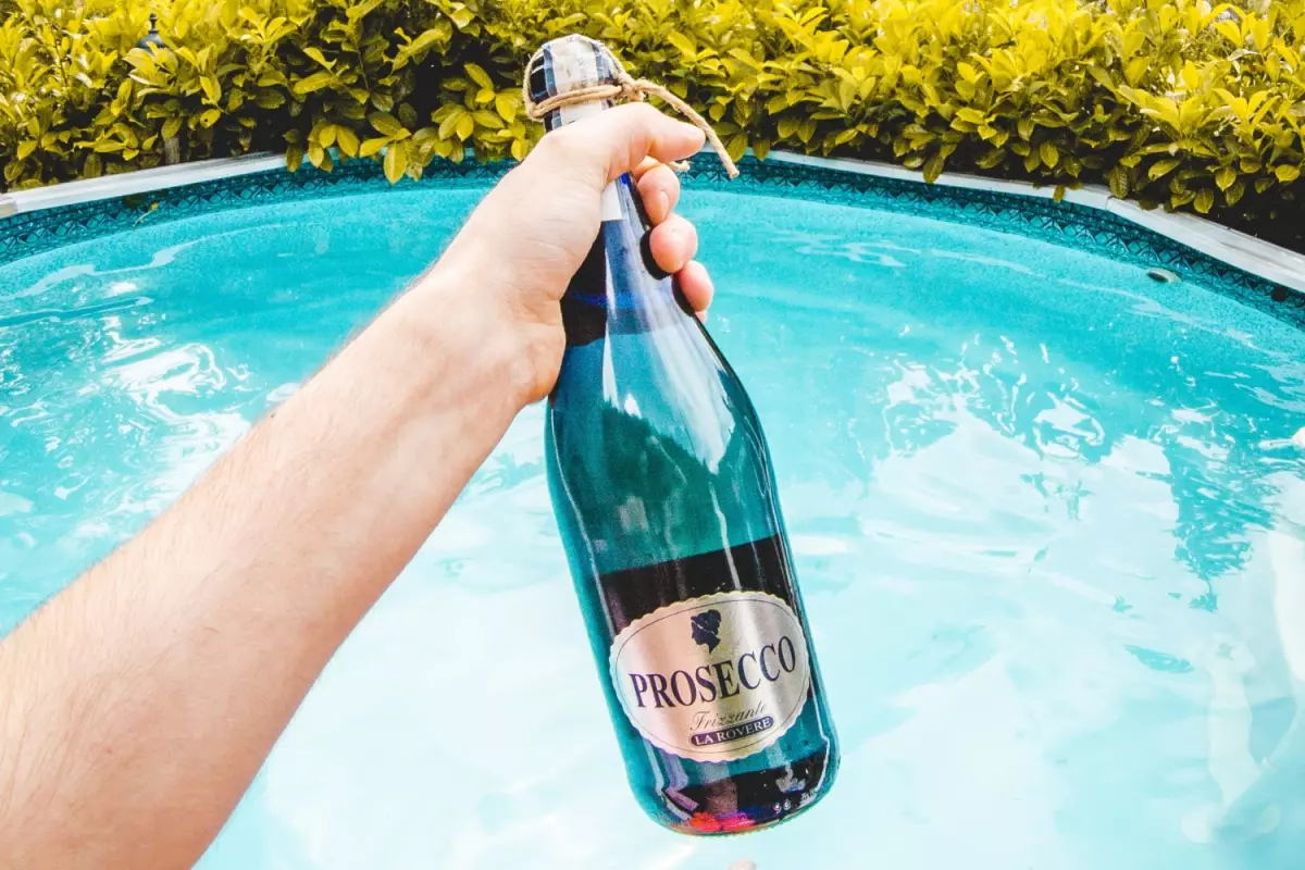 ọkunrin dani igo prosecco pẹlu kan pool ni abẹlẹ