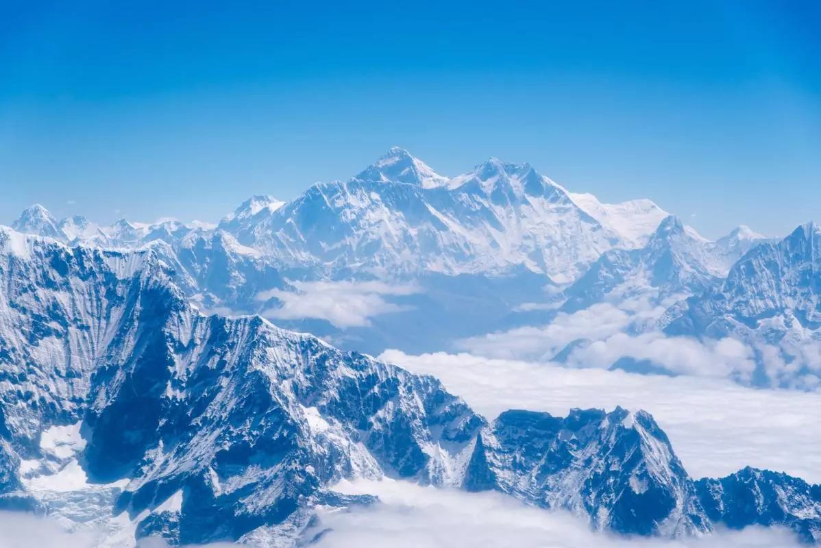 Le mont Everest enneigé photographié de loin surplombant d'autres sommets sous un ciel bleu