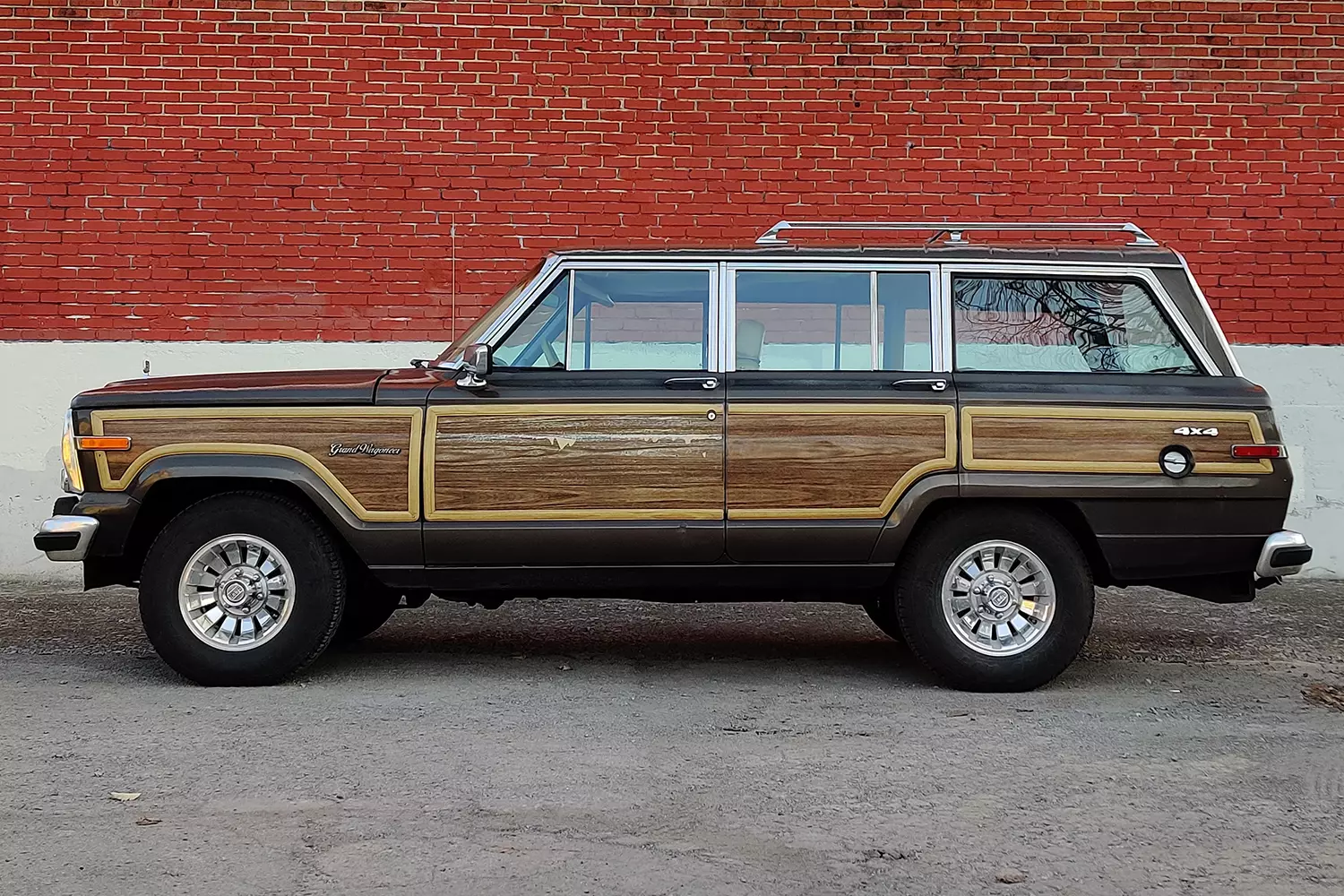 Кызыл кирпеч стенага 1987-нче елда Jeep Grand Wagoneer-ның ян профиле