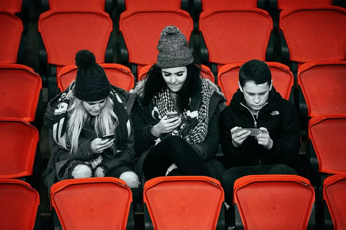 Professional futbol o'yini tribunalarida uchta yosh o'zlarining aqlli telefonlarini ko'rishmoqda