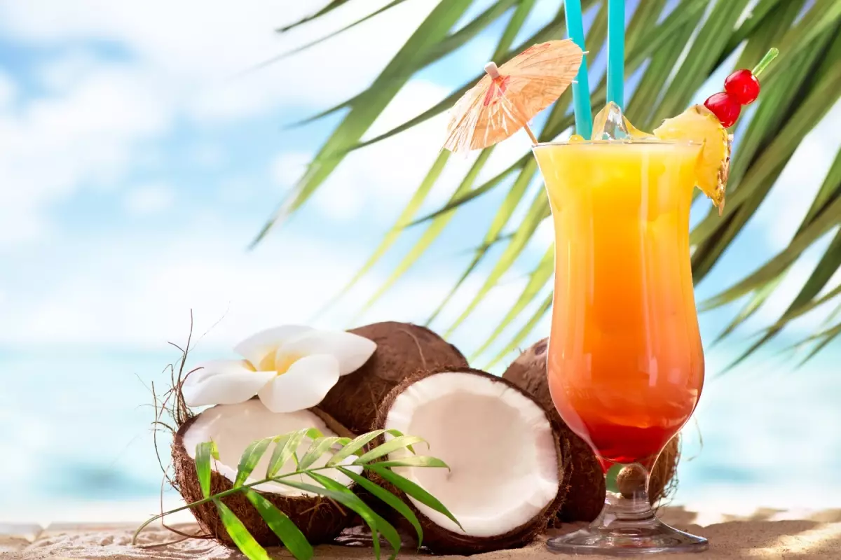 Een kleurrijke sex op het strand cocktail naast wat kokosnoten. Strandscène op de achtergrond.