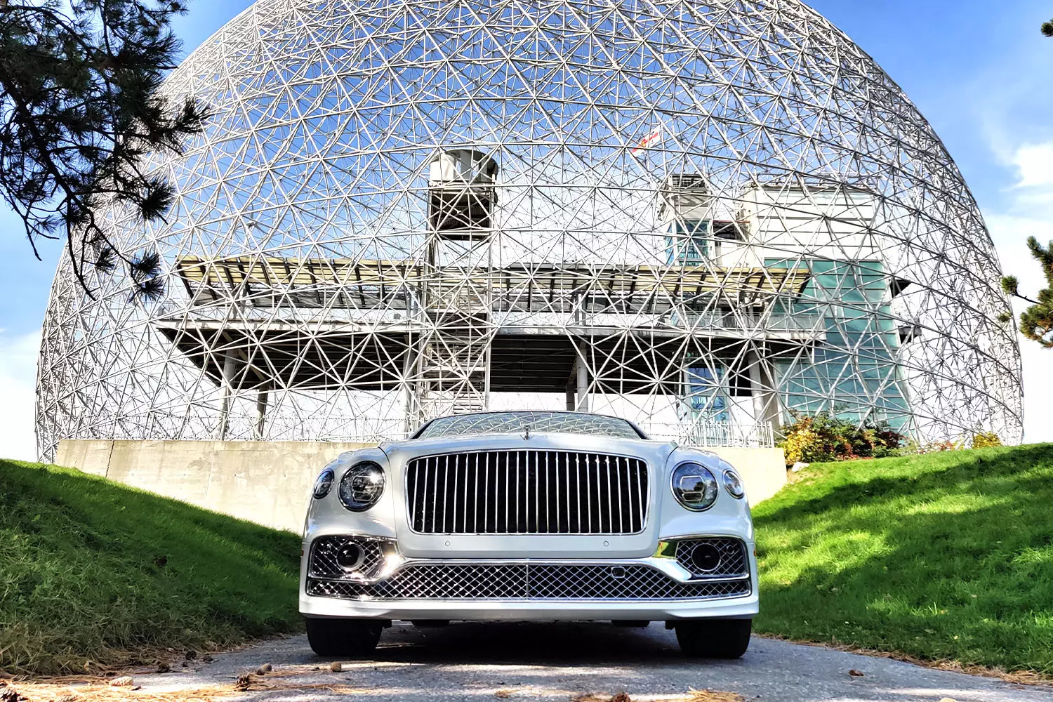 Bentley Flying Spur од 2022 година во бело пред биосферата во Монтреал со купола дизајнирана од Бакминстер Фулер