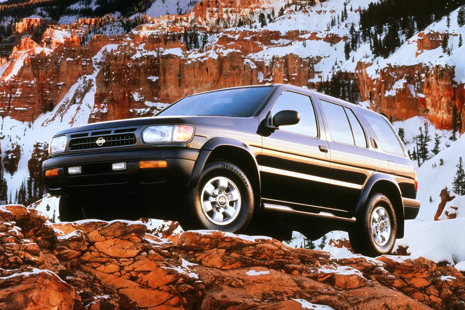 SUV Nissan Pathfinder 1997 bertengger di gunung dengan batu tertutup salju di latar belakang dalam foto vintage