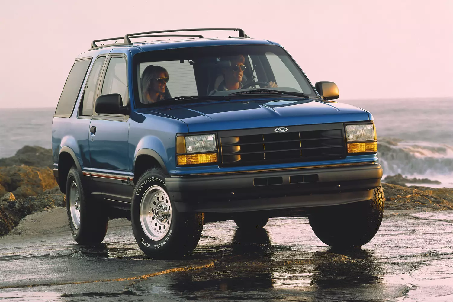 Seorang pria mengendarai SUV Ford Explorer berwarna biru tahun 1992 di dekat laut dalam foto vintage