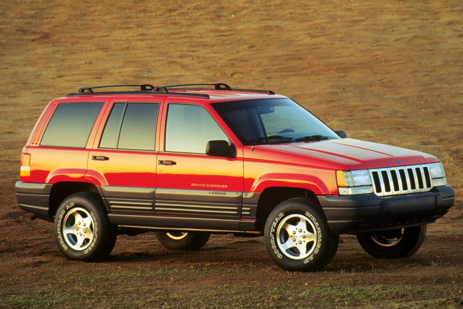 'n 1996 Jeep Grand Cherokee Laredo in rooi wat op die grond sit in 'n vintage foto