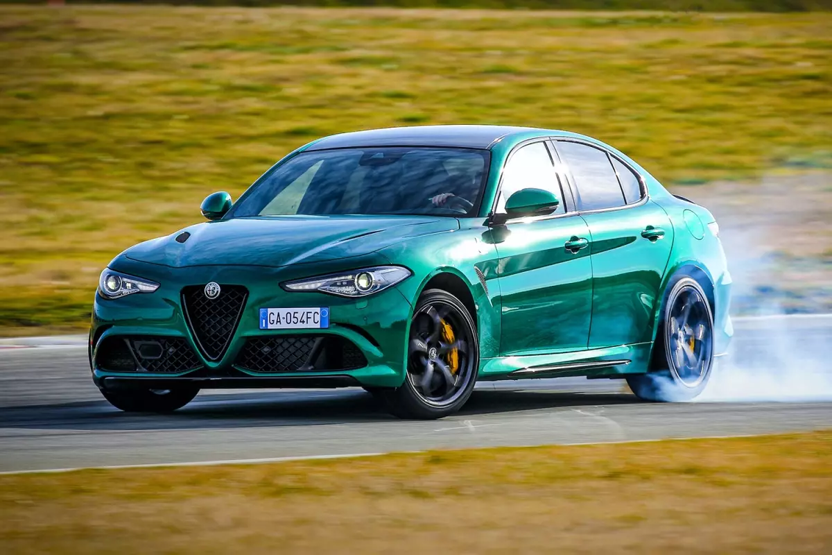 Egy zöld, 2021-es Alfa Romeo Giulia Quadrifoglio sportlimuzin füstölög a gumiabroncsokon a fűvel körülvett versenypályán