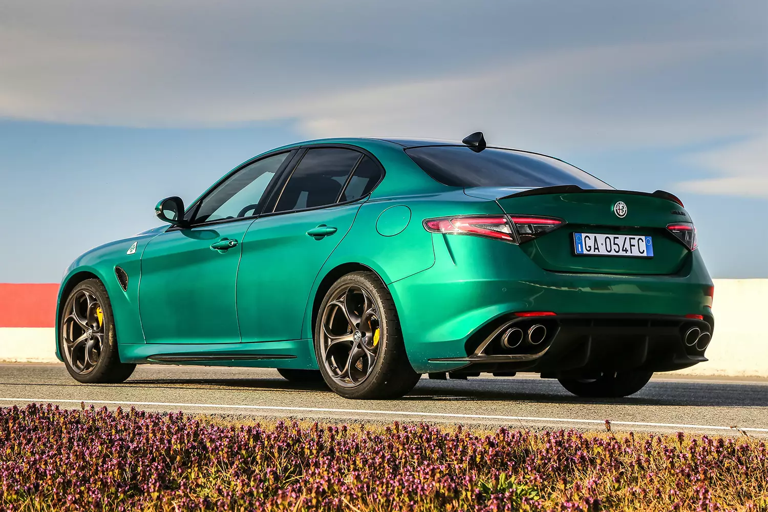 Sportowy sedan Alfa Romeo Giulia Quadrifoglio 2021 w zielonym ujęciu z tyłu po lewej stronie, siedzący na torze wyścigowym otoczonym trawą