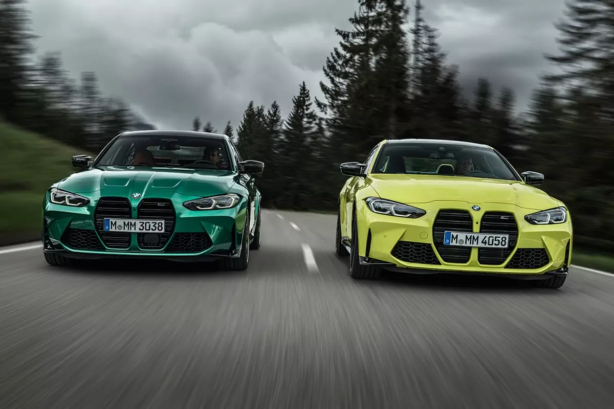 2021 BMW M3 Competition-ի կանաչ սեդան ձախ կողմում արագ վարում է 2021 BMW M4 Competition Coupe-ի կողքին՝ դեղին գույնով աջ կողմում՝ ծառերը երևում են ետին պլանում։