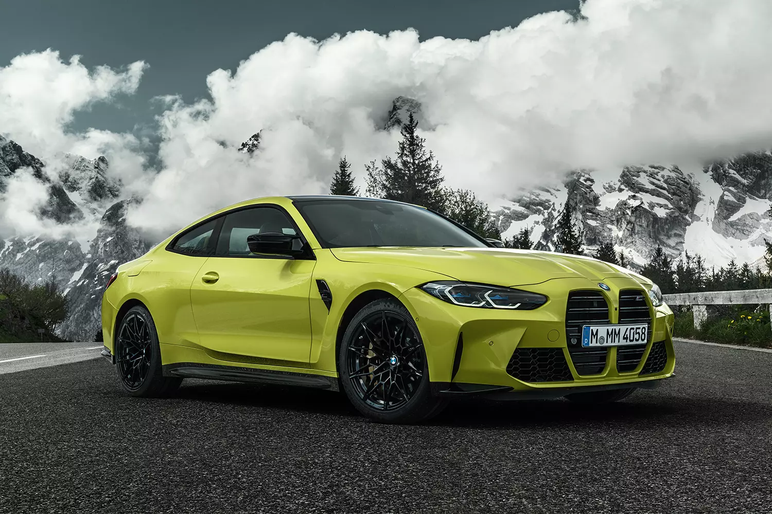 Նոր BMW M4 Competition Coupé-ն դեղին գույնով նստած է ճանապարհի վրա՝ ձնառատ լեռներով և ծառերով՝ ամպի գծի հետին պլանում: