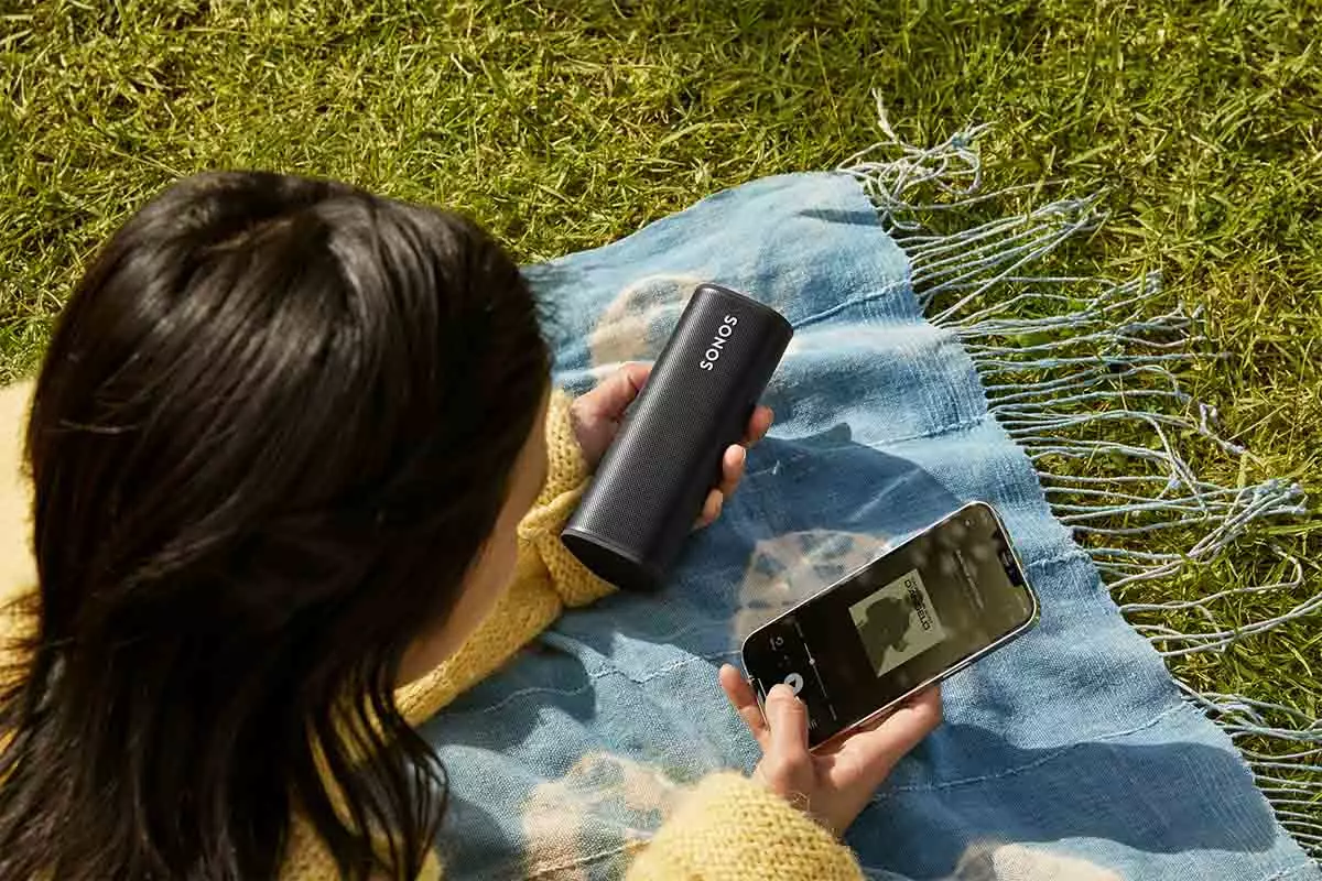 Uma mulher emparelhando seu telefone com um Sonos Roam enquanto está sentada em um cobertor em um parque