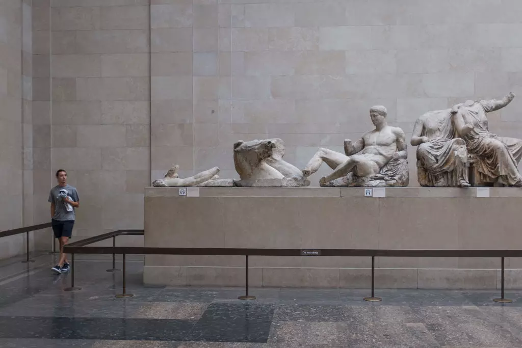 Siúlann cuairteoir timpeall na Marmar Parthenon (Elgin) i Seomra 18 de Mhúsaem na Breataine, ar 12 Meitheamh 2018, i Londain, Sasana. (Grianghraf le Richard Baker / In Pictures via Getty Images Images)